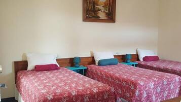 Quarto de hotel com três camas, cada uma com colcha e almofadas estampadas. Há um quadro na parede acima das camas.