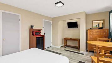 Quarto de hotel com cama, escrivaninha com cadeira, cômoda, micro-ondas e televisão.