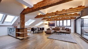 Ampla área de estar estilo loft, com vigas de madeira aparentes, sala de jantar e cozinha com eletrodomésticos modernos.