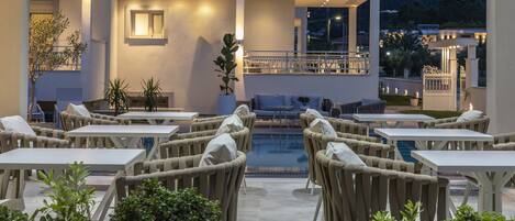 Uma área externa com mesas, cadeiras, piscina e plantas em vasos.