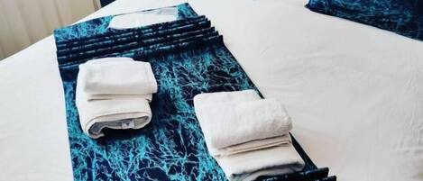 Cama bem arrumada com colcha estampada em azul, travesseiros brancos e cabeceira.