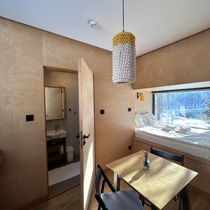 Quarto moderno com decoração em madeira, uma cama com vista para uma paisagem nevada, uma pequena mesa com um vaso e um lustre.