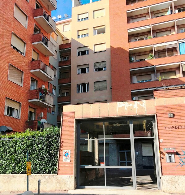 Um edifício residencial com vários andares, varandas, entrada com portão e sinalização de proibição de estacionamento.