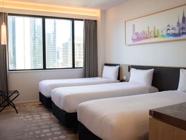 Quarto de hotel com duas camas, uma pintura de paisagem urbana na parede e vista para edifícios pela janela.