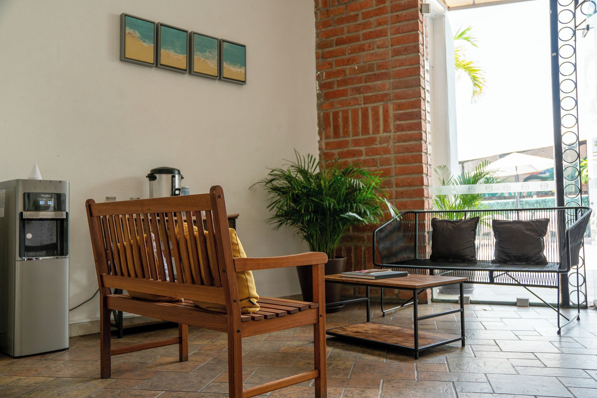 Um espaço de estar acolhedor com um banco de madeira, uma mesa de metal, um frigorífico e uma planta em vaso.