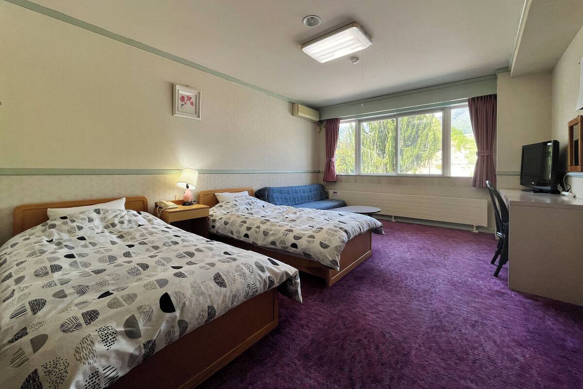 Quarto de hotel com duas camas, uma escrivaninha, televisão e uma janela com cortinas.