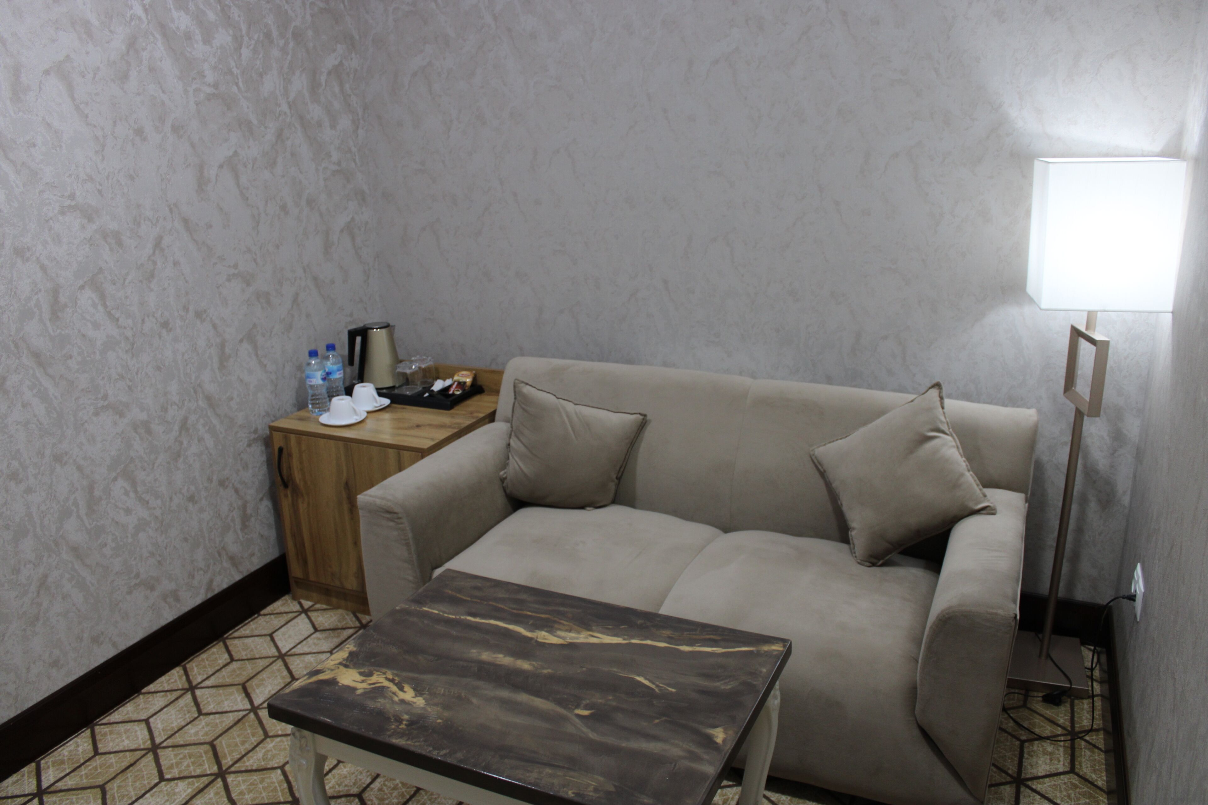 Um quarto com sofá, uma mesa de madeira pequena, luminária e piso de azulejos.