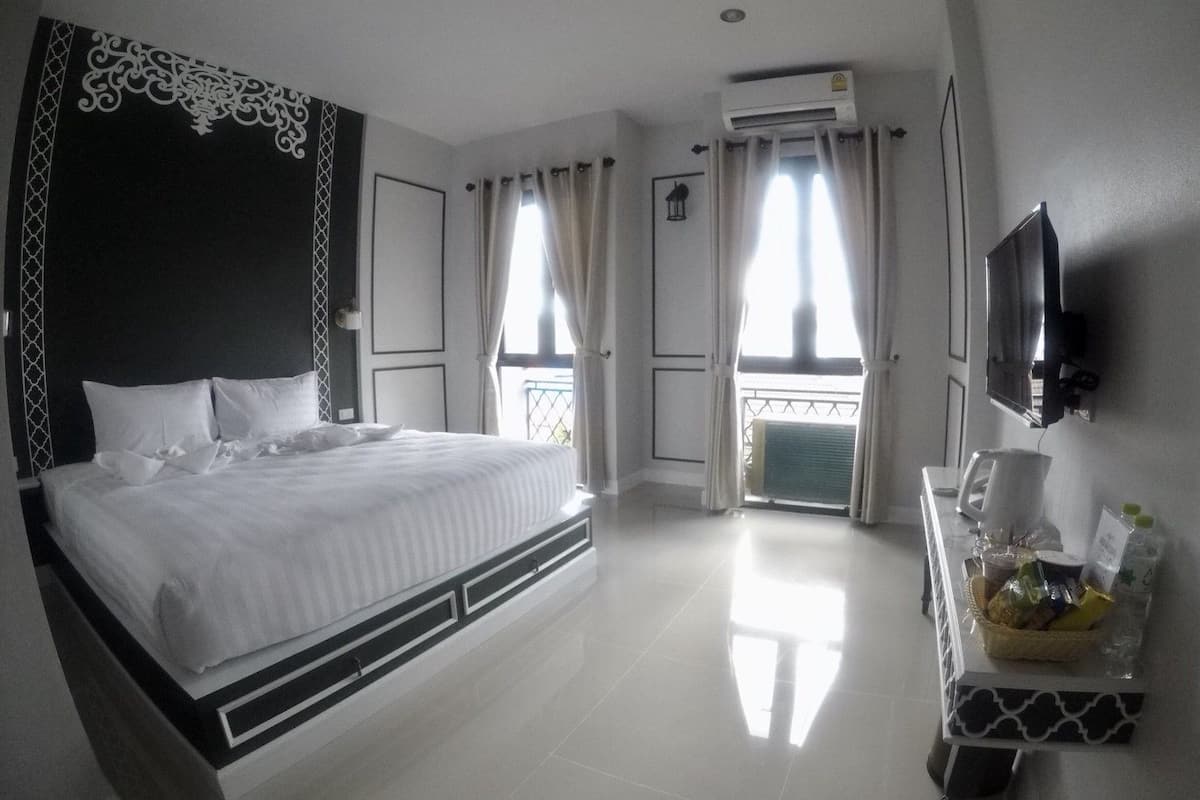 Quarto de hotel com uma cama grande, uma televisão, aparelho de ar condicionado e uma varanda com cortinas.