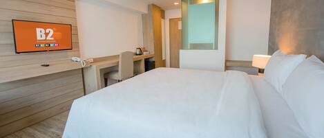 Quarto de hotel com cama, escrivaninha, cadeira, televisão fixada na parede e espelho.