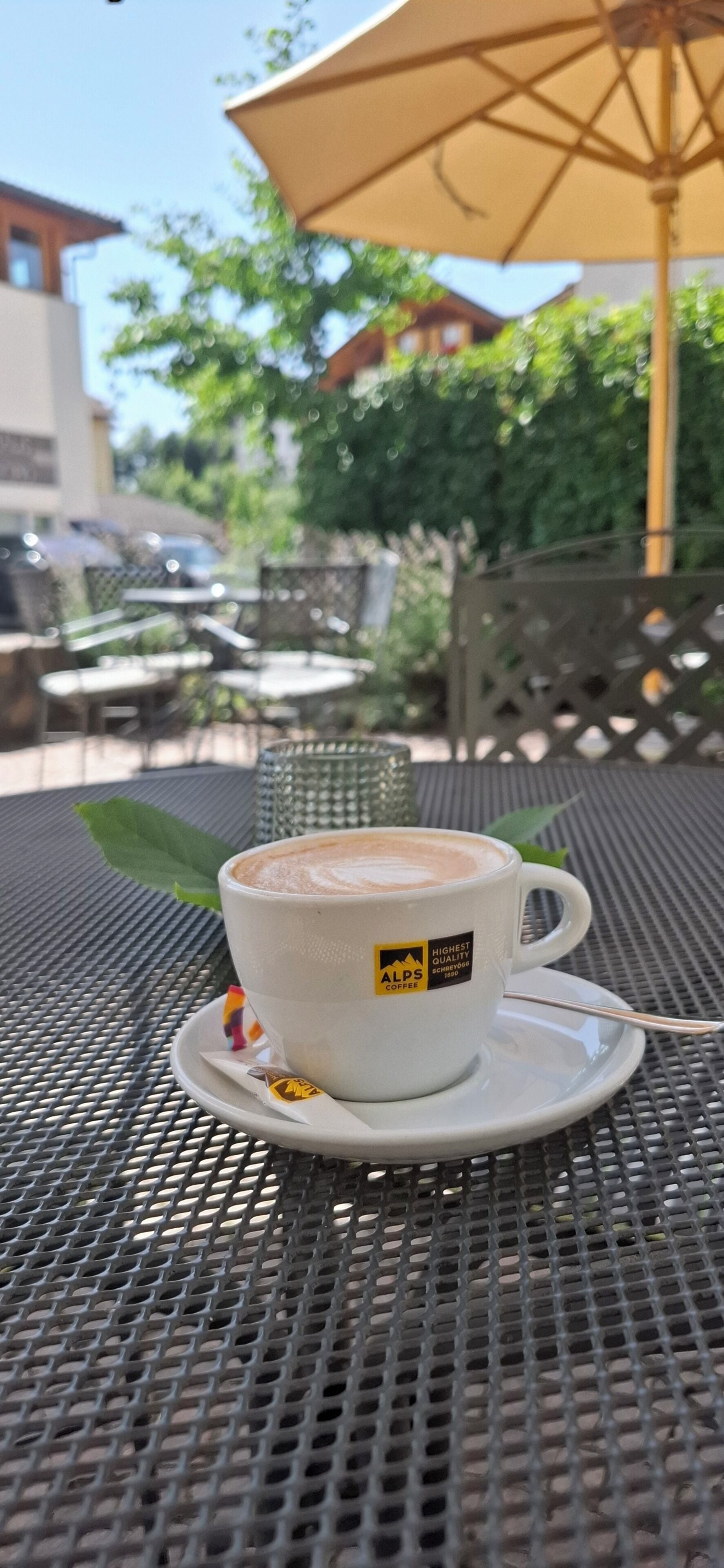 Uma chávena de café sobre uma mesa de metal com uma etiqueta, sob um toldo.