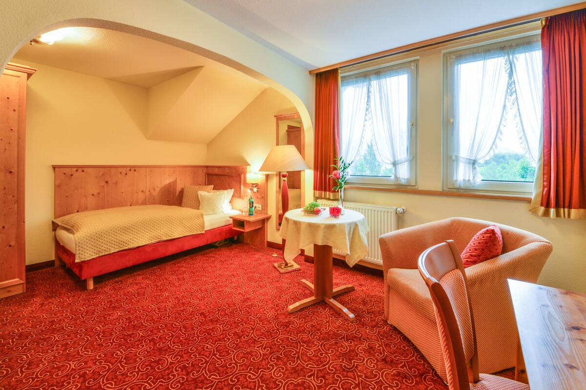 Quarto com cama, cadeira, mesa e janela com cortinas.