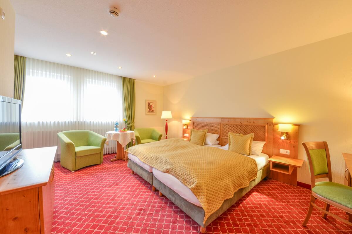 Quarto de hotel com uma cama grande, uma escrivaninha, uma cadeira, uma mesinha e uma televisão.