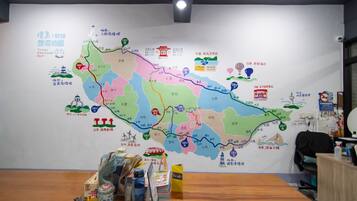 Mapa na parede com rotas de viagem e dias indicados, uma mesa com diversos objetos e uma cadeira.
