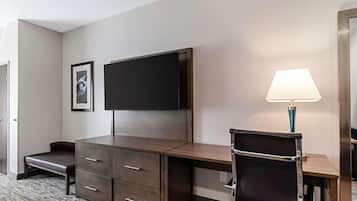 Quarto de hotel com uma secretária de madeira, televisão de tela plana, um banco, uma luminária e um quadro emoldurado na parede.