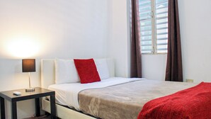 Quarto bem arrumado com cama, mesa de cabeceira com abajur e janela com cortinas.