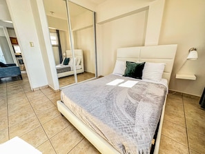 Quarto com cama grande, mesa de cabeceira, espelho e vista para a cozinha.