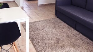 Uma sala de estar moderna com um sofá escuro, uma mesa branca e um laptop em uma escrivaninha.