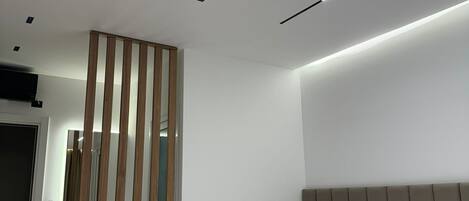 Quarto moderno com cama, divisória de madeira e teto com iluminação embutida.