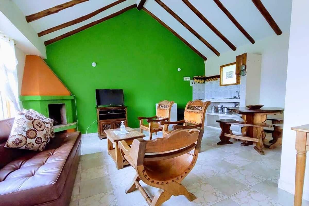Uma sala de estar com parede verde, móveis de madeira, lareira e televisão.