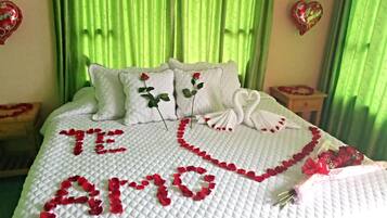 Uma cama com pétalas de rosa dispostas formando a frase 'Te Amo' e dois cisnes feitos de pétalas.