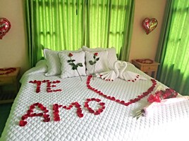 Uma cama com pétalas de rosa dispostas formando a frase 'Te Amo' e dois cisnes feitos de pétalas.