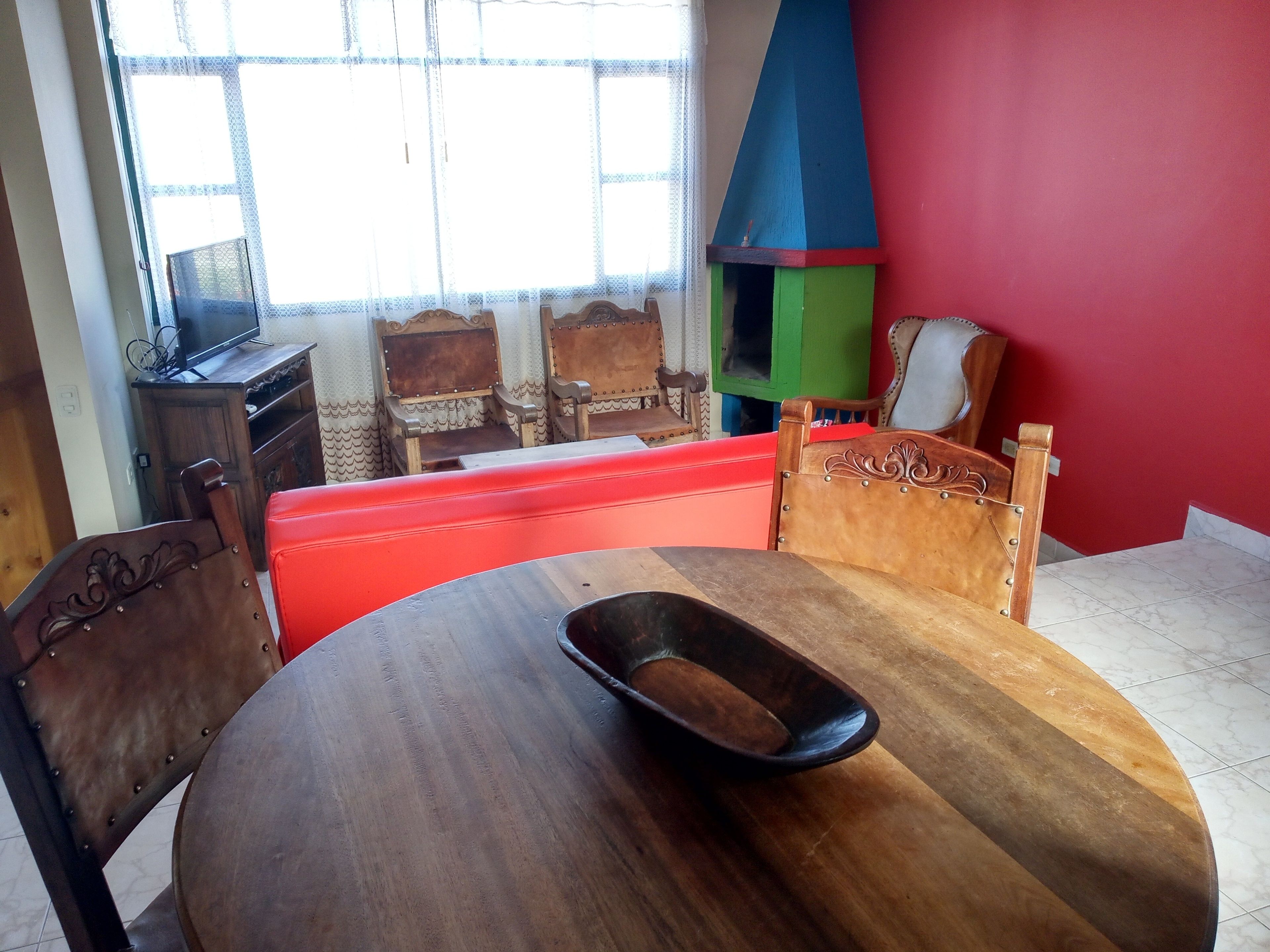 Uma área de refeições com mesa de madeira, cadeiras e um banco vermelho.