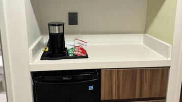 Uma cozinha compacta com micro-ondas na prateleira superior, cafeteira e máquina de lavar louça embaixo.