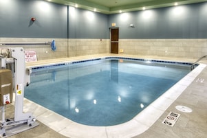 Piscina com cadeira do salva-vidas, um aviso de segurança e uma porta ao fundo.