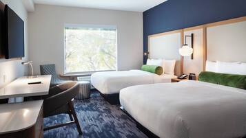 Quarto de hotel com escrivaninha, duas camas, uma janela grande e vista para árvores.