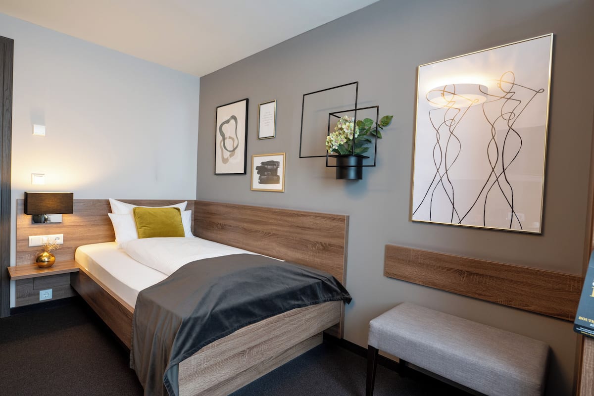 Quarto de hotel com cama, mesa de cabeceira, luminária, obras de arte na parede e um banco.
