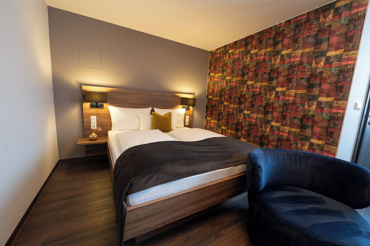 Quarto de hotel com uma cama, mesas de cabeceira, uma cadeira e um papel de parede estampado.