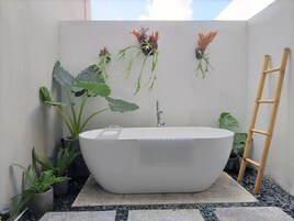 Um banheiro moderno com uma banheira livre, uma escada de bambu e diversas plantas em vasos.