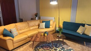 Uma sala de estar com um sofá amarelo, um sofá azul, uma mesa de centro de madeira e um tapete estampado.
