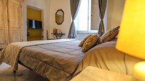 Quarto com cama, televisão, espelho e janela com cortinas.