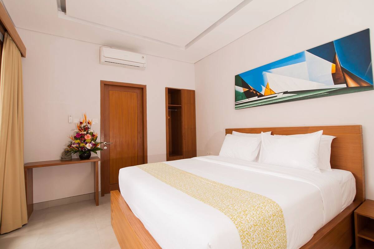Quarto de hotel com cama, escrivaninha, guarda-roupa e um quadro na parede.