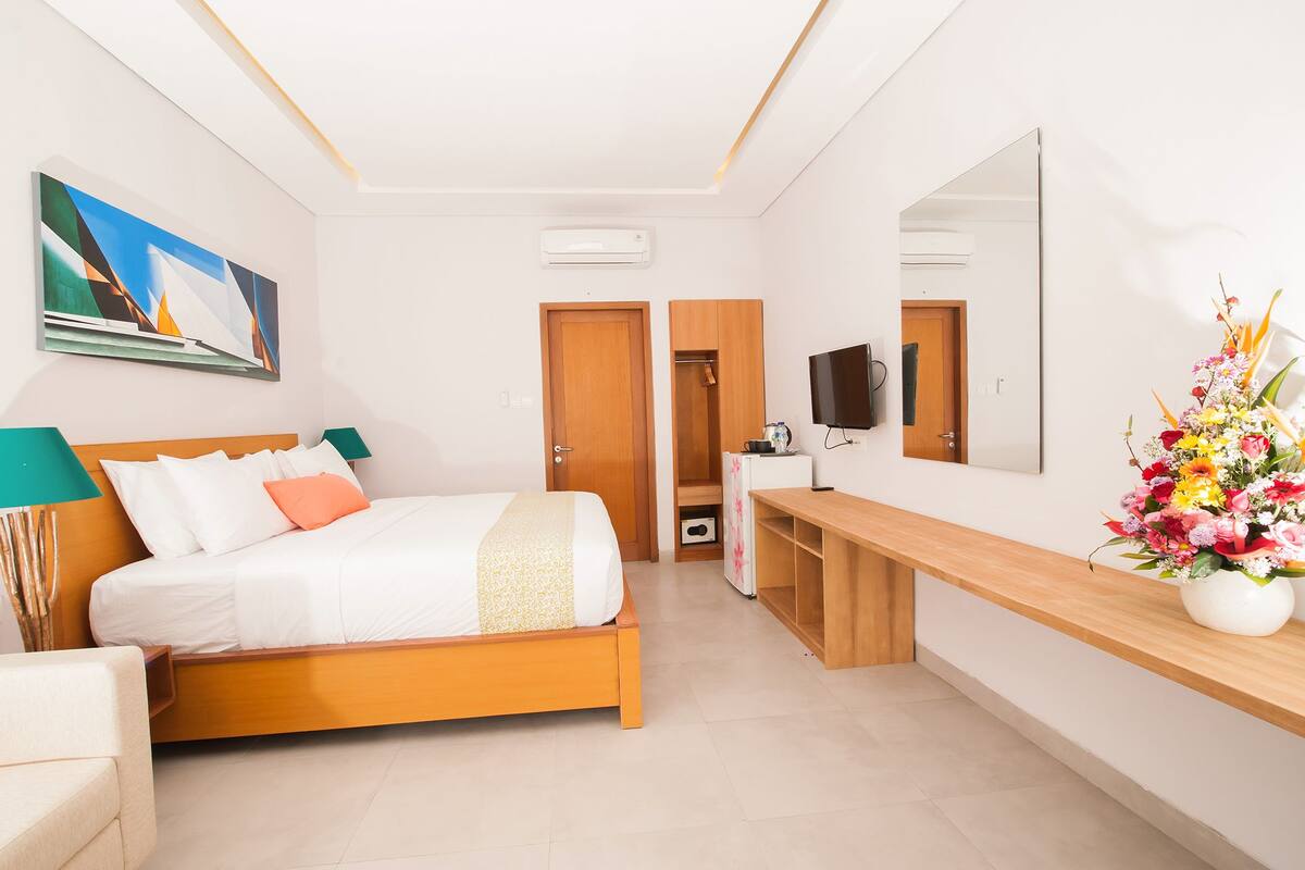 Quarto de hotel moderno com cama, secretária, televisão e espelho.