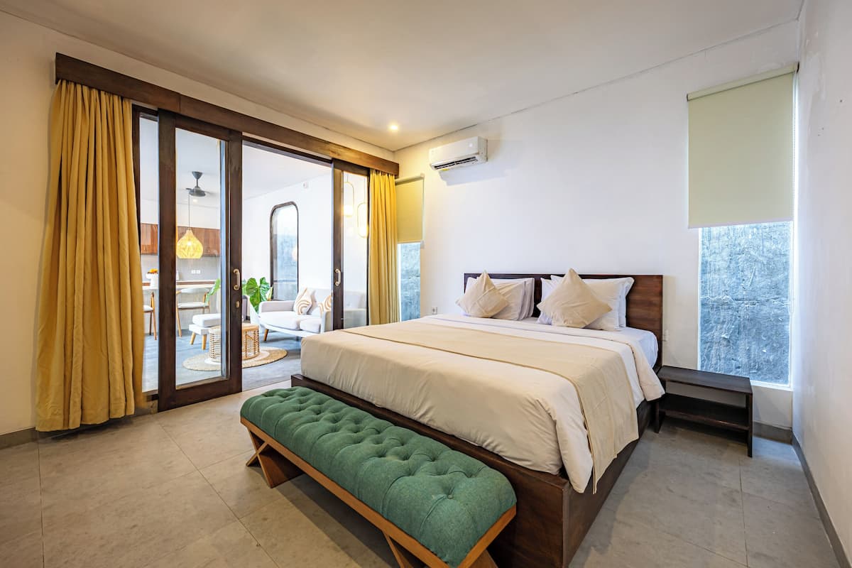 Quarto com cama, banco, porta de correr e vista para o exterior.