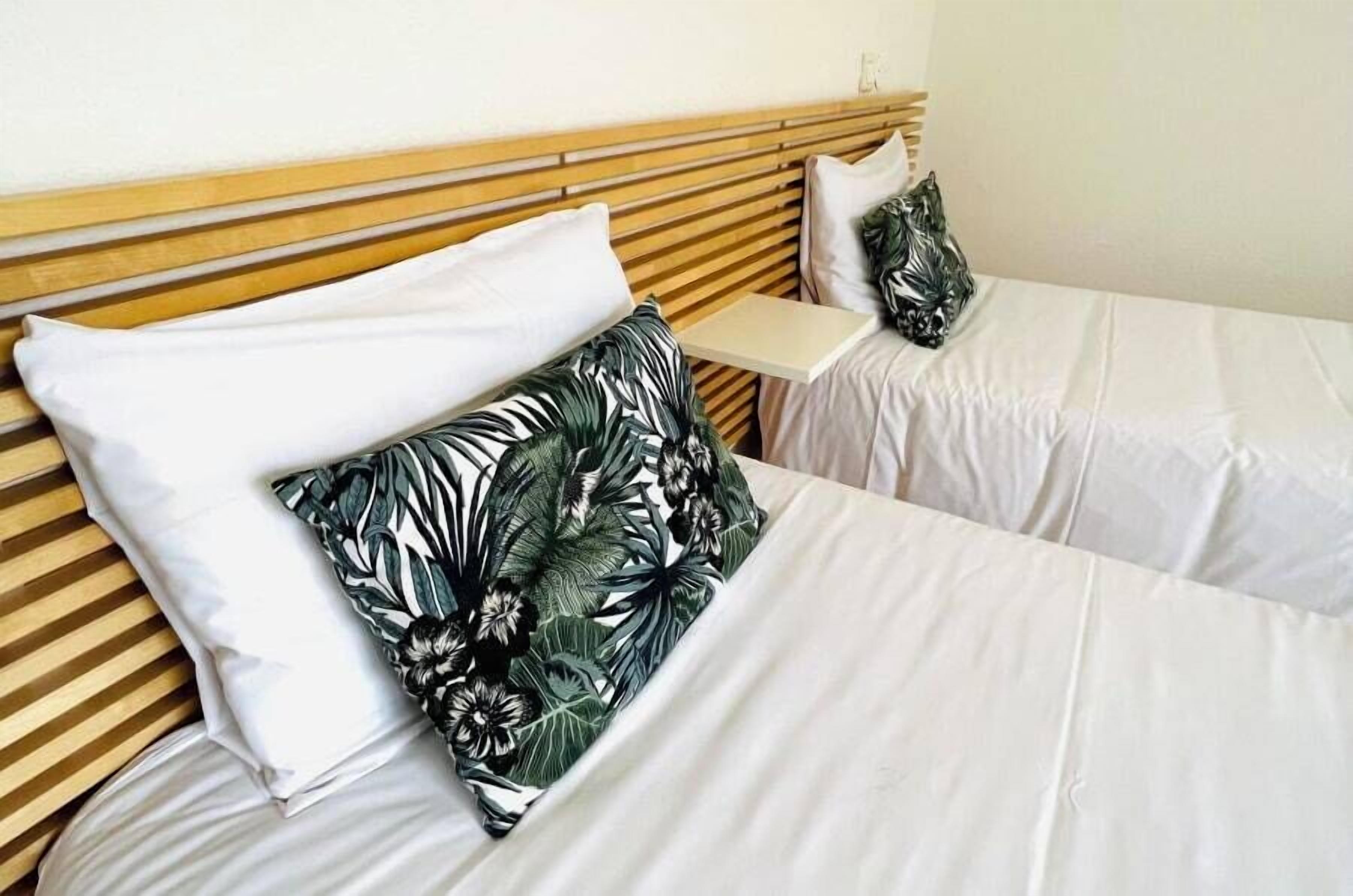 Quarto de hotel com duas camas, cada uma com roupa de cama branca e cabeceira de madeira.