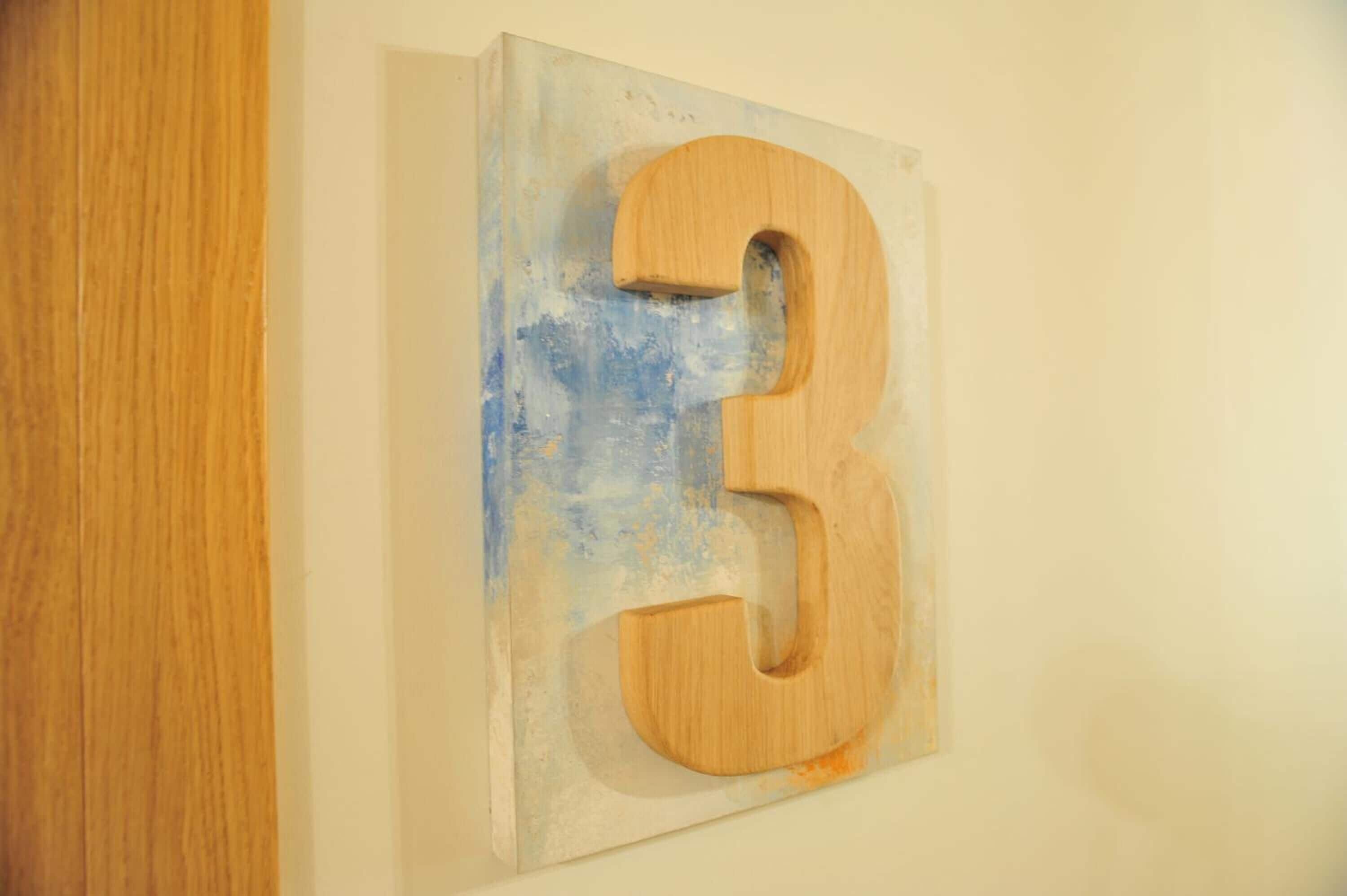 Um número '3' de madeira fixado na parede, com fundo em tinta azul desgastada.