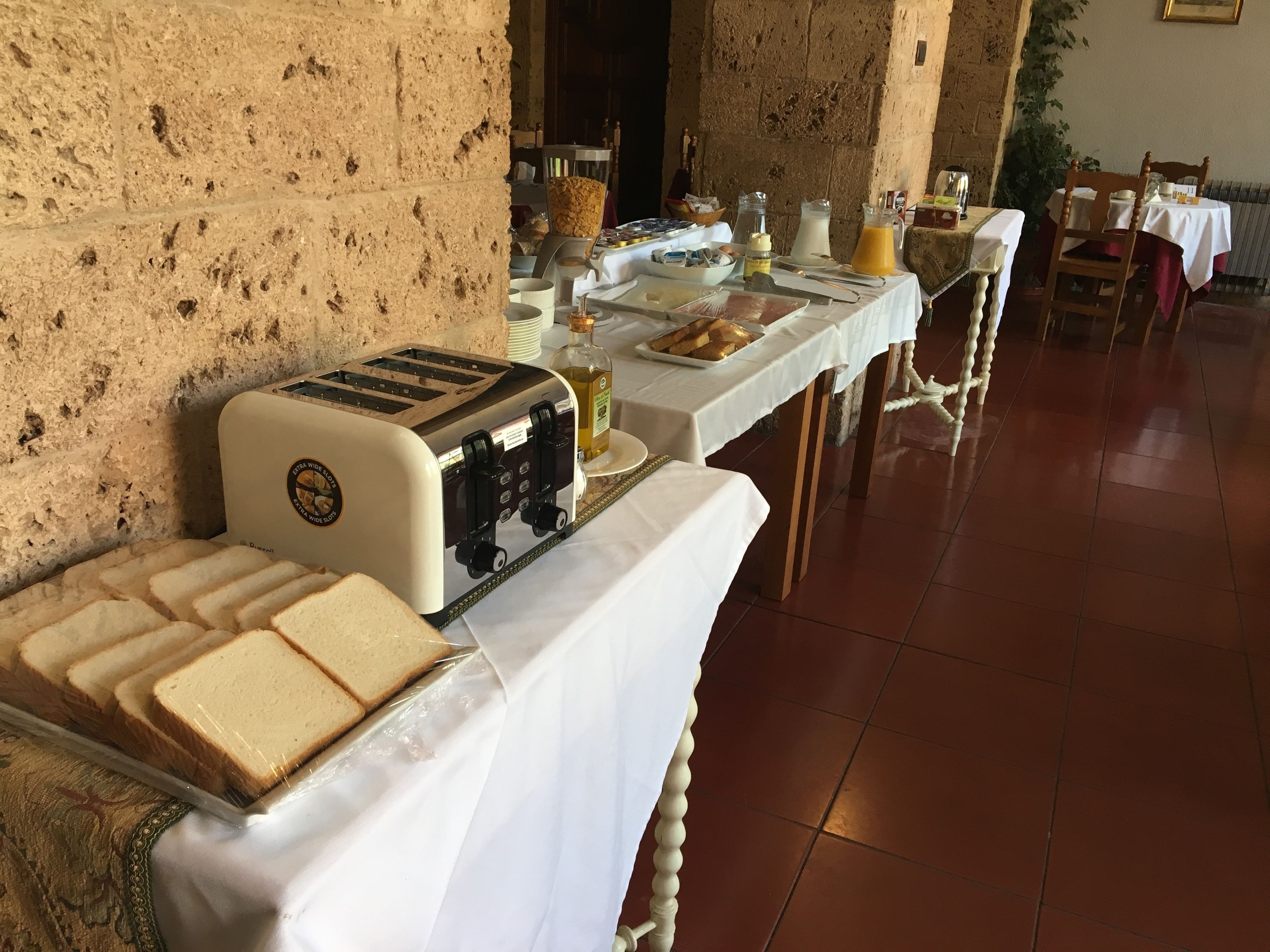 Disposição de buffet de café da manhã com uma torradeira, pão e diversos itens para o café da manhã sobre uma mesa.