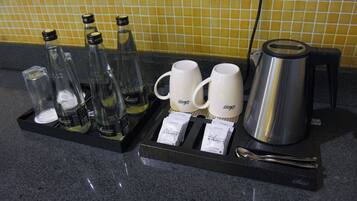 Uma bandeja com garrafas, canecas brancas e uma cafeteira de prata sobre um balcão.