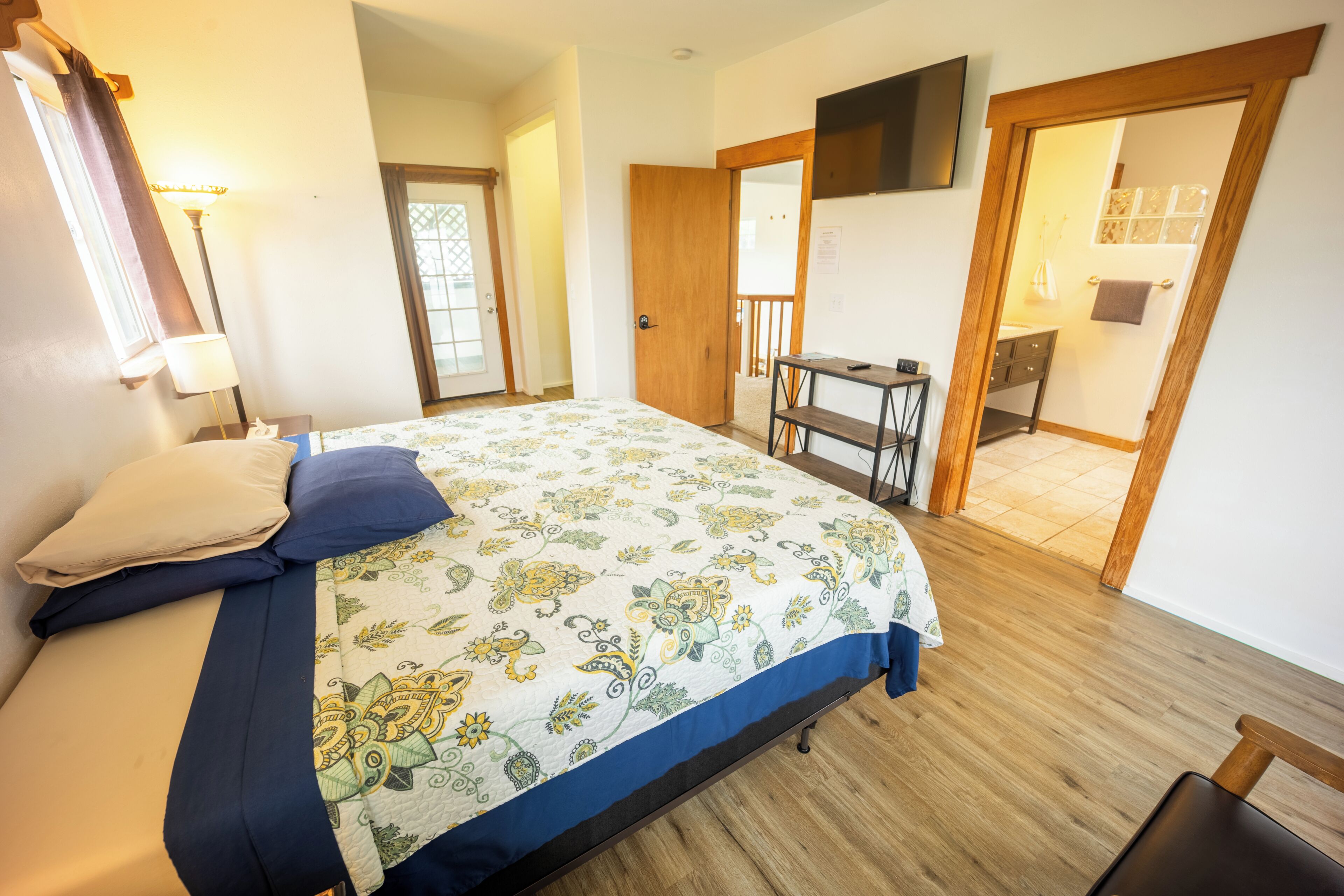 Quarto com cama, escrivaninha e banheiro visível por uma porta aberta.