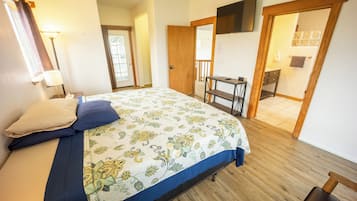 Quarto com cama, escrivaninha e banheiro visível por uma porta aberta.