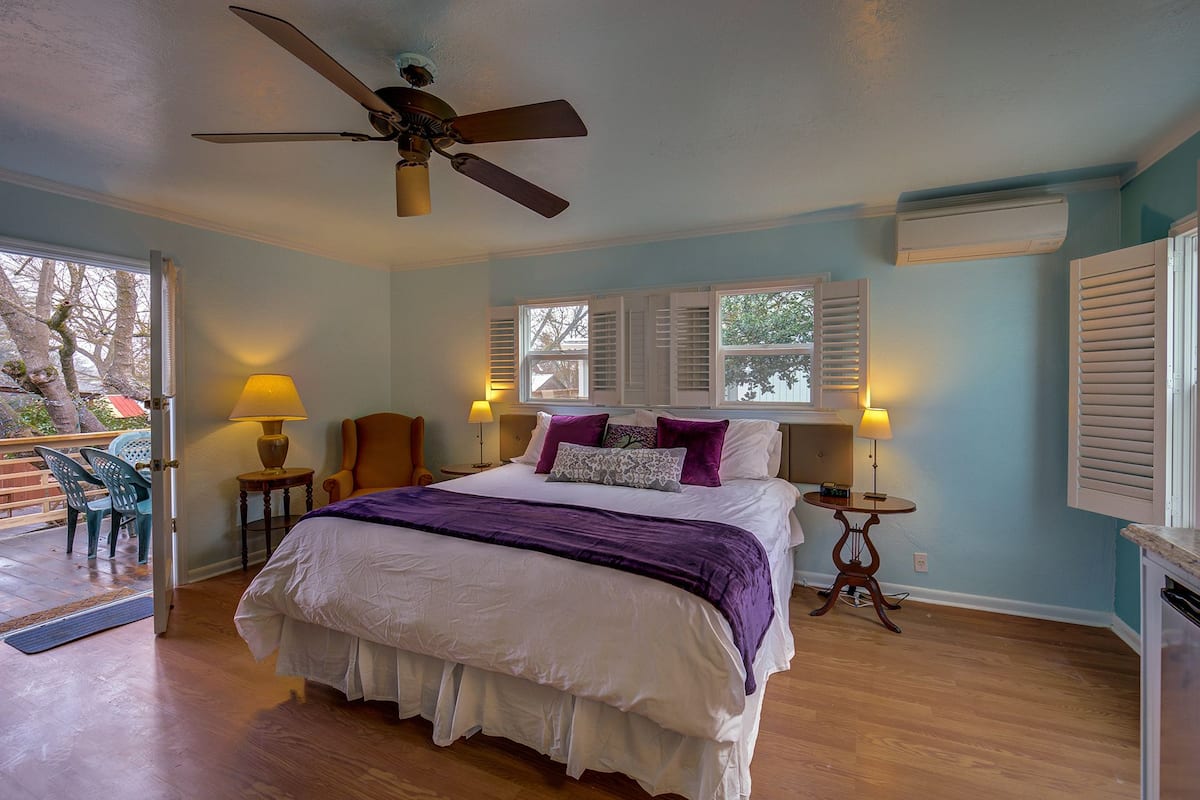 Quarto com uma cama, duas mesas de cabeceira, um ventilador de teto e uma janela com persianas.