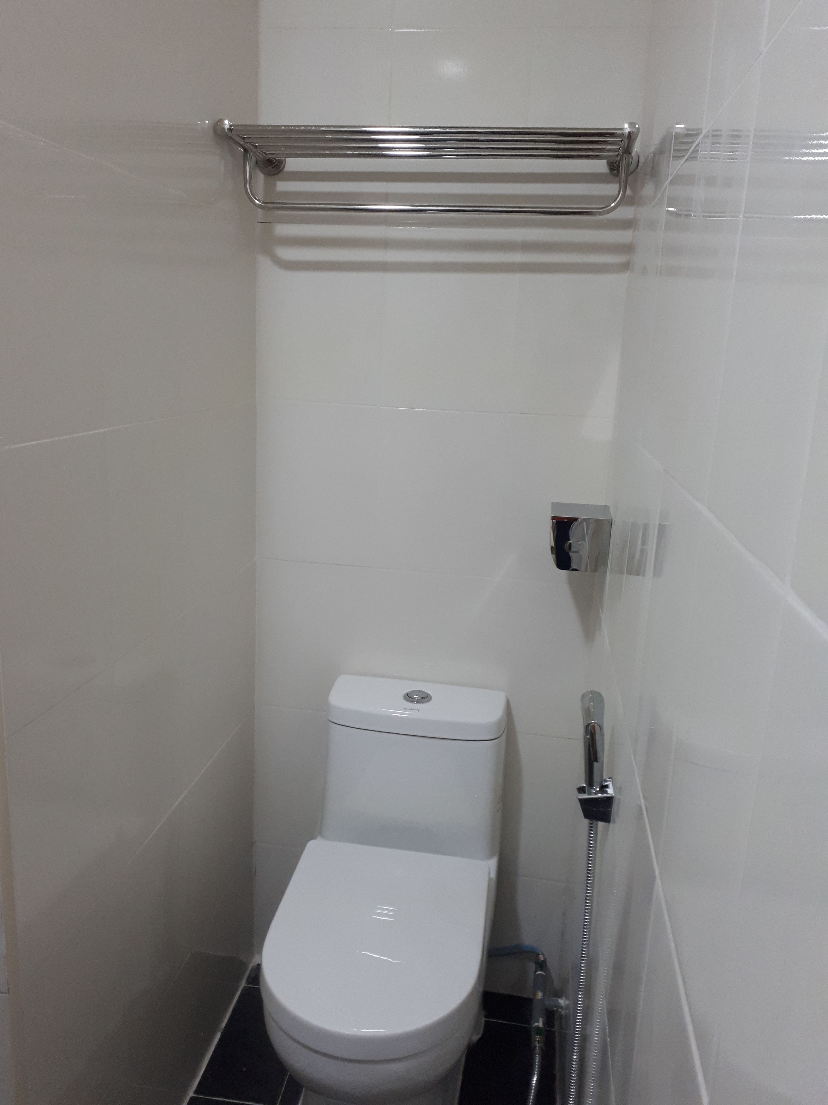 Um banheiro pequeno e moderno, com vaso sanitário branco, porta-toalhas cromado e controle de chuveiro.