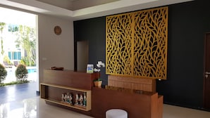 Uma área de recepção com um balcão de madeira, um painel decorativo e um pequeno vaso de planta.