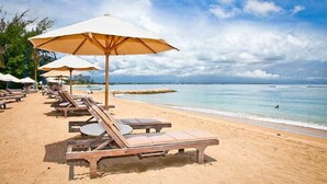 Uma praia com espreguiçadeiras e guarda-sóis, céu claro e o oceano ao fundo.