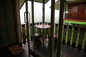 Uma área externa coberta com uma mesa e cadeiras de madeira, um tapete verde e uma cerca decorativa.