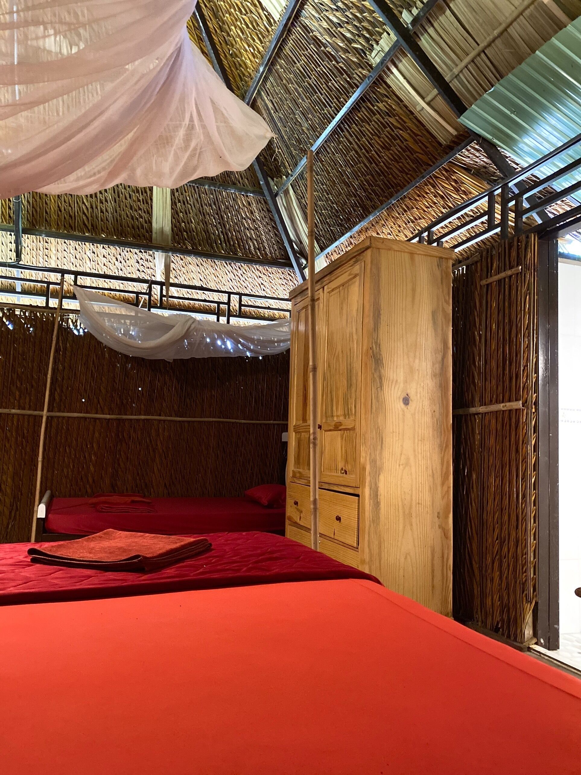 Um quarto com telhado de palha, guarda-roupa de madeira e roupa de cama vermelha.
