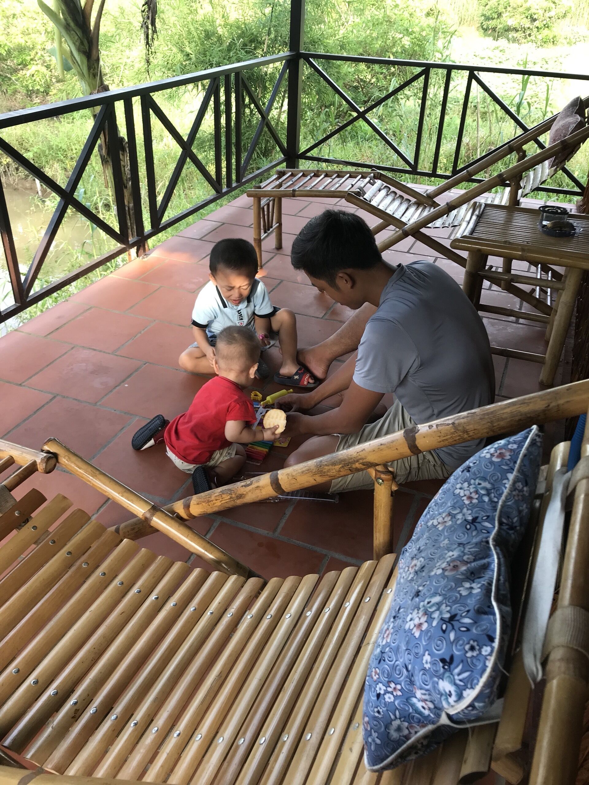 Uma área de estar coberta ao ar livre, com guarda-corrimão de bambu, uma mesa e um banco estofado.
